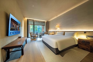 Quarto de hotel moderno com uma cama grande, um banco de madeira, uma escrivaninha e uma televisão fixada na parede.