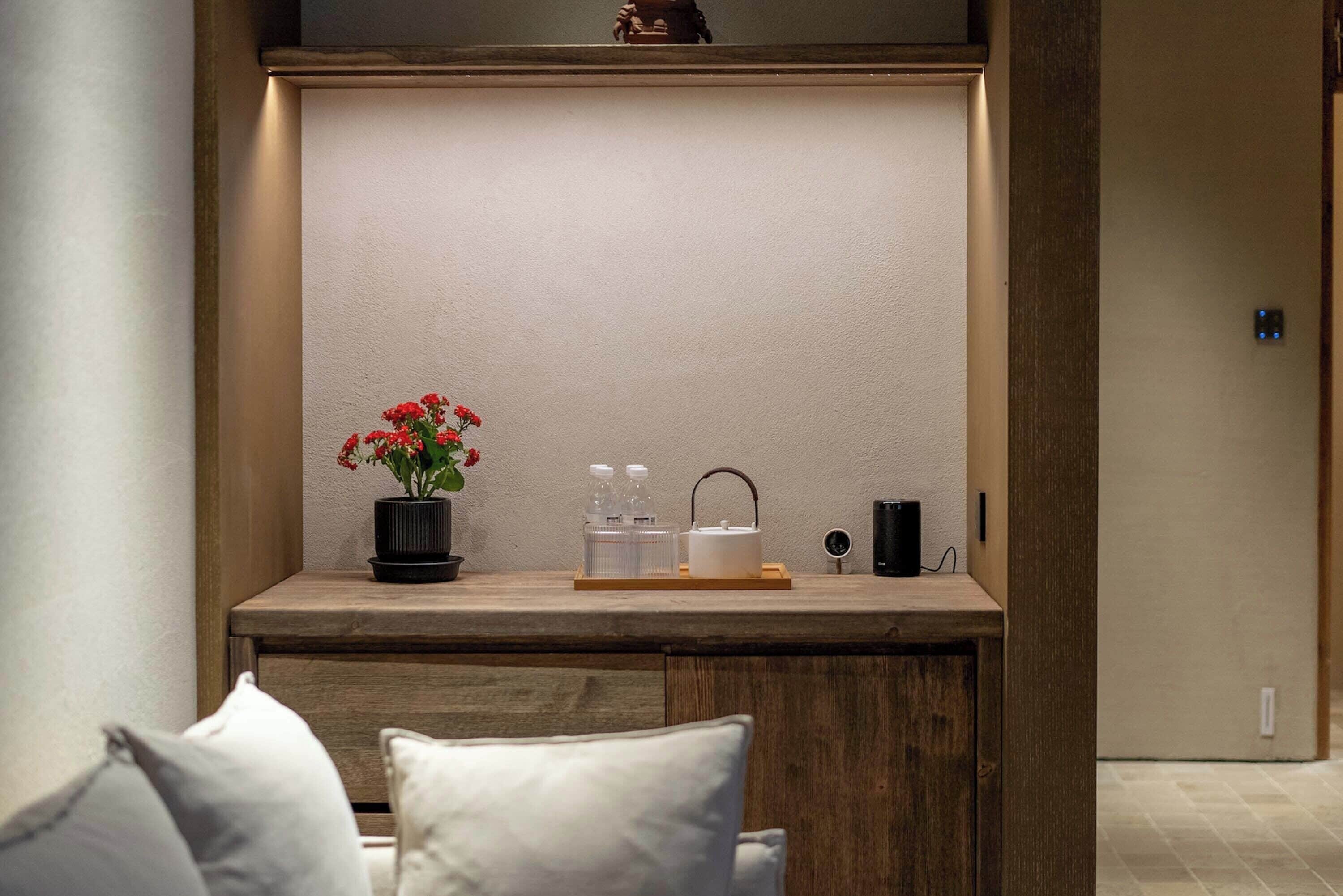 Quarto moderno com escrivaninha de madeira, um vaso com flores vermelhas, chaleira e um pequeno tabuleiro com garrafas.