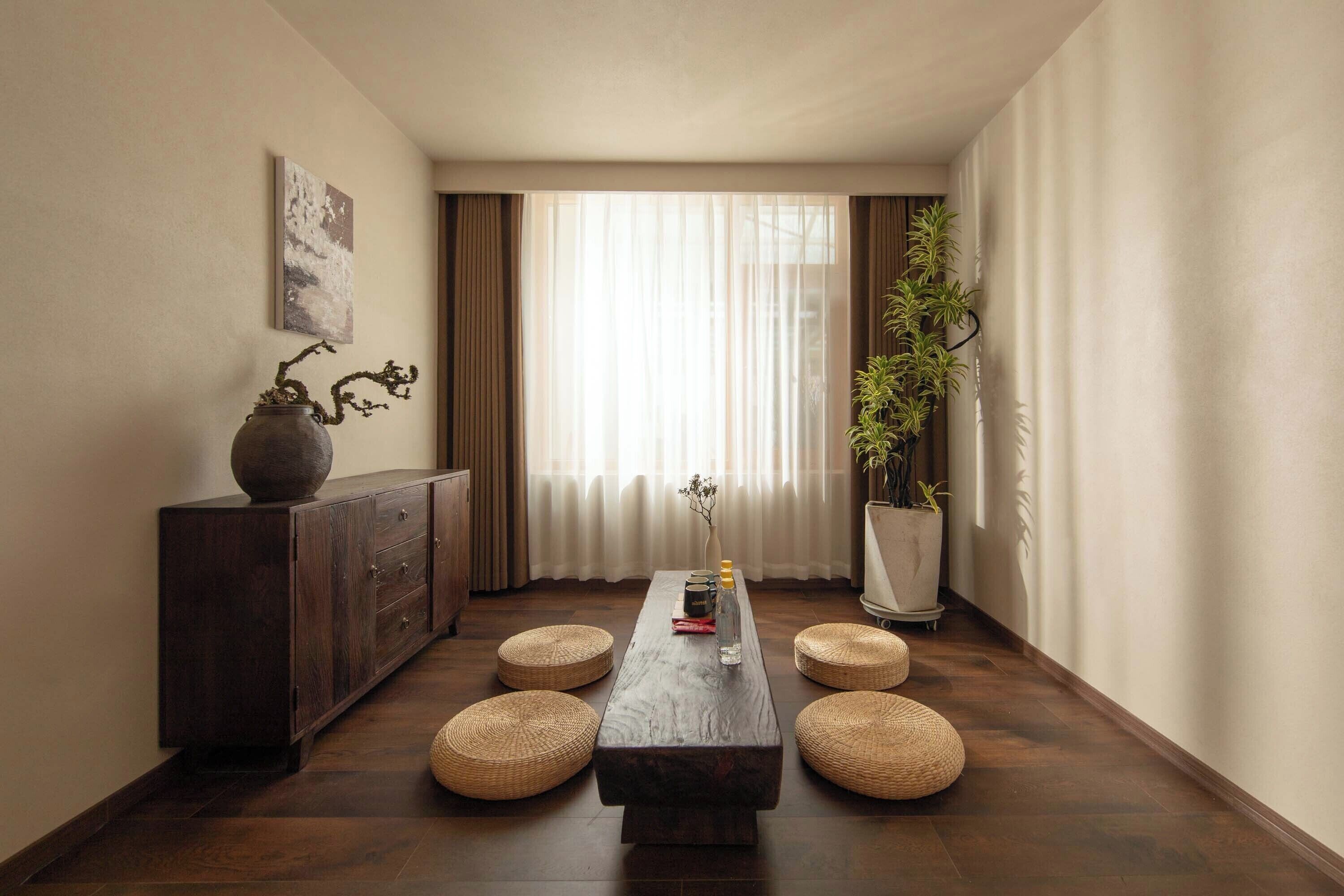 Quarto com uma mesa de madeira, quatro pufes trançados, um armário, um vaso e uma planta em vaso.