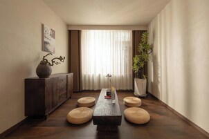 Quarto com uma mesa de madeira, quatro pufes trançados, um armário, um vaso e uma planta em vaso.