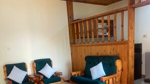 Um quarto com duas poltronas de madeira com almofadas verdes, uma mesa de centro de madeira e um tapete estampado com padrão de zebra.