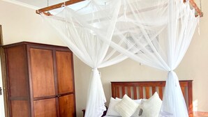 Uma cama de dossel com cortina, cabeceira de madeira e roupa de cama branca.