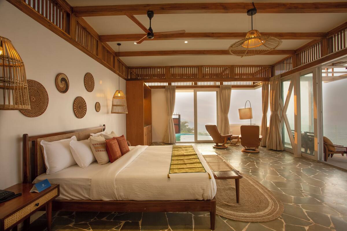 Um quarto espaçoso com uma cama grande, vigas de madeira no teto e vista para o oceano através de grandes portas de correr.