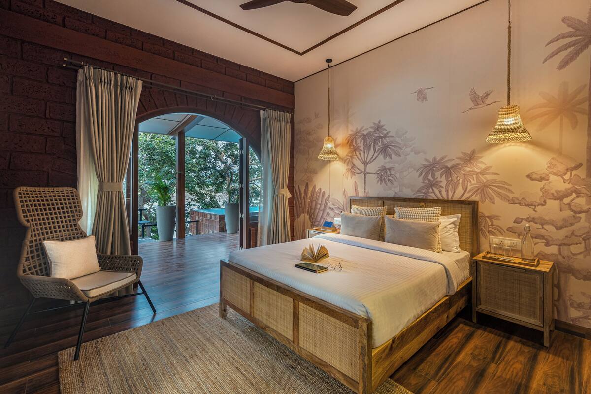 Quarto com uma cama grande, uma cadeira, uma mesa de cabeceira e vista para o exterior.