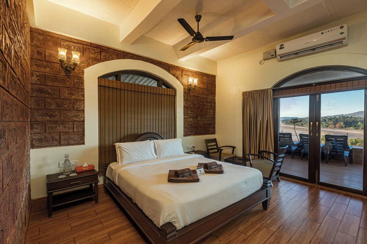 Quarto de hotel com uma cama grande, ventoinha no teto, aparelho de ar condicionado e vista para o exterior.