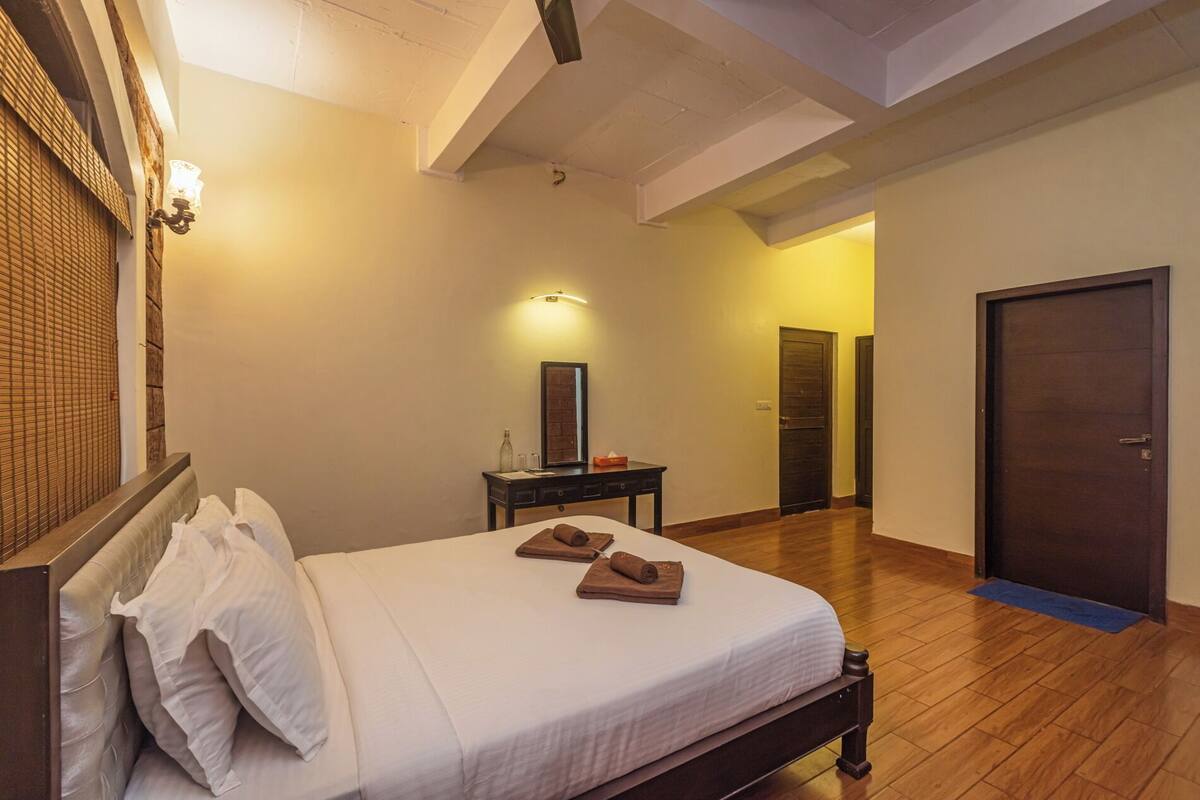 Quarto de hotel com cama, mesa de cabeceira, espelho e porta.
