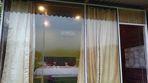Quarto com cama, cortinas e porta de vidro deslizante para uma varanda.