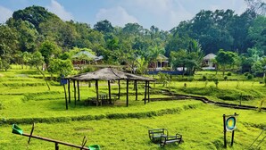 Paisagem rural com um pavilhão de colmo, um balanço e uma mesa pequena.