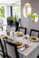 Uma sala de jantar com uma mesa posta para quatro pessoas, com pratos de massa e saladas, copos de vinho e um vaso de flores.