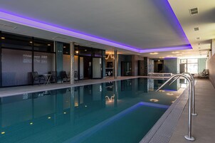 Piscina interior com barreira de vidro, área de estar e iluminação moderna.