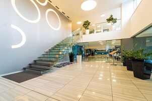 Um interior moderno com escadaria de vidro, piso lustroso e plantas em vasos.