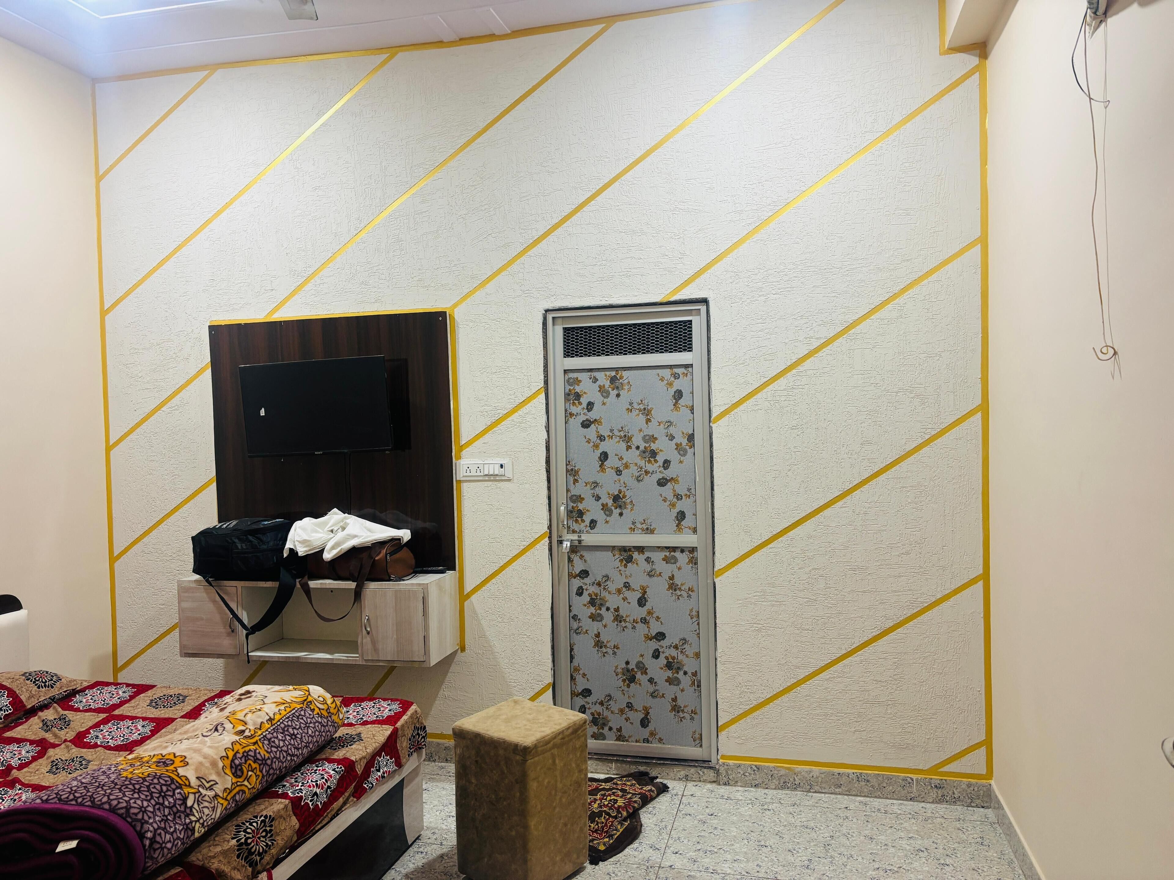 Quarto com cama, televisão fixada em um painel de madeira, guarda-roupa e porta com padrão floral.