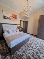 Uma cama grande com cabeceira escura, um candelabro, um quadro na parede e um tapete estampado.