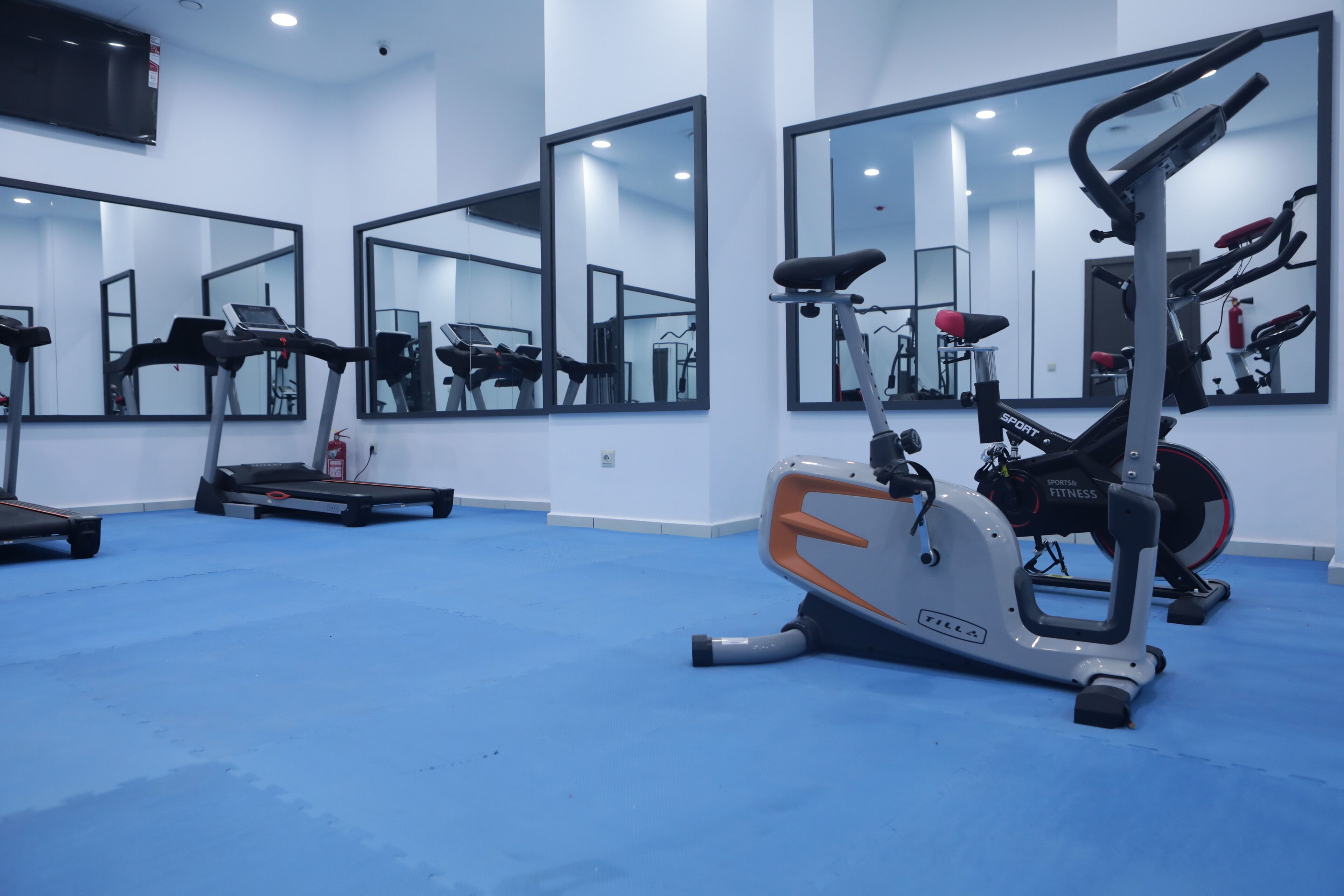 Uma academia com equipamentos de exercício, espelhos grandes e chão azul.