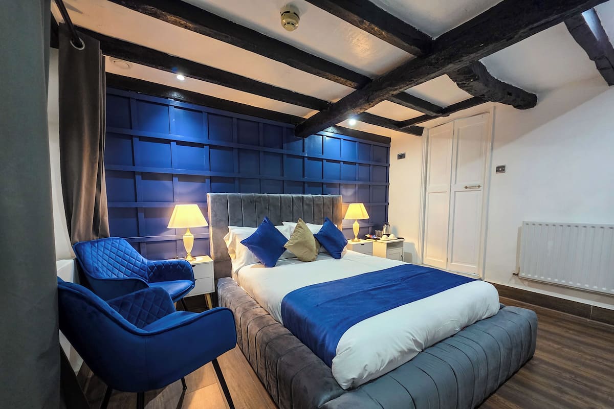 Quarto moderno com uma cama grande, duas mesas de cabeceira com luminárias, uma cadeira azul e um guarda-roupa.