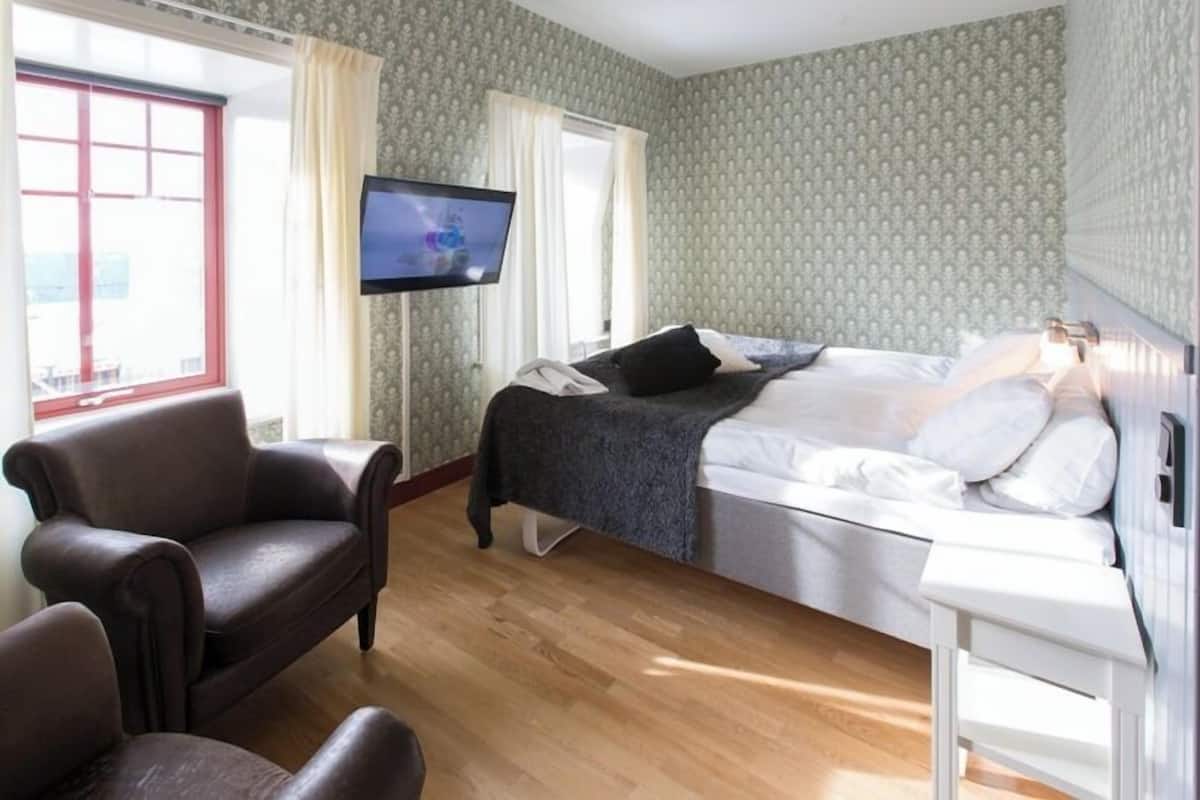 Quarto de hotel com cama, televisão, poltrona e escrivaninha.