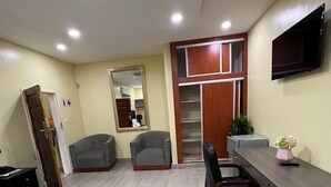 Quarto de hotel compacto com cama, escrivaninha, cadeira e televisão fixada na parede.
