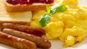 Um prato com ovos mexidos, salsichas, torradas com geleia e um raminho de hortelã.