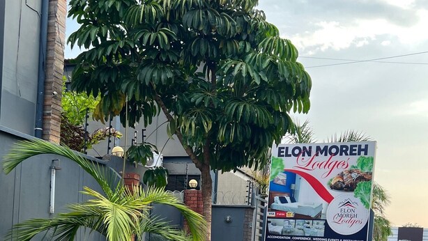 Uma área ajardinada com um caminho de pedra, uma palmeira e um letreiro de Elon Moreh Lodges anunciando hospedagem, eventos de conferência, casamentos e um restaurante.