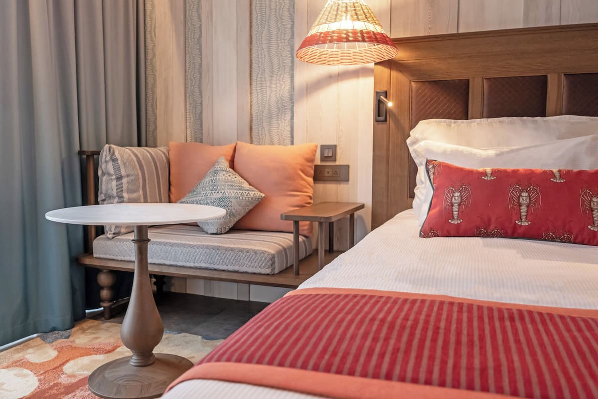 Quarto de hotel bem arrumado, com cama, uma pequena mesa redonda e um sofá com almofadas.