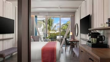 Quarto de hotel com cama, escrivaninha, cadeira, televisão e varanda com vista para palmeiras.