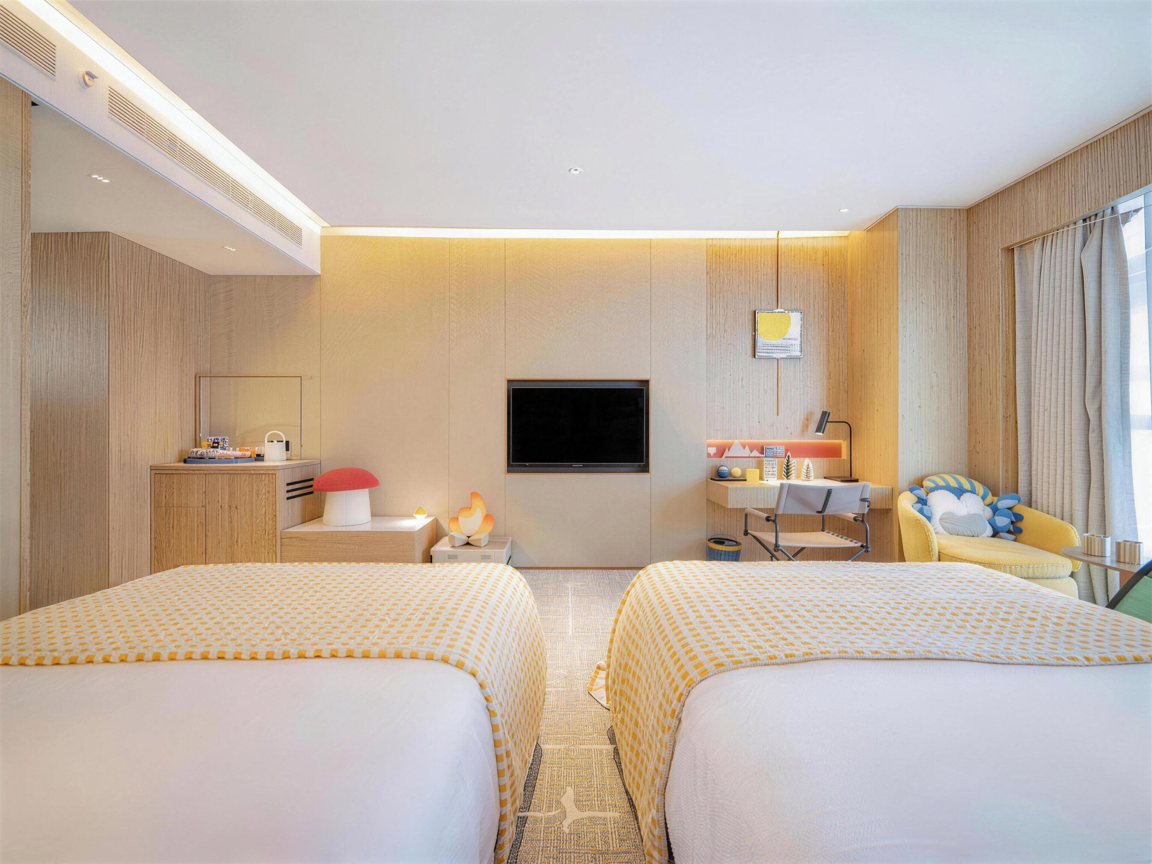 Quarto de hotel com duas camas, uma escrivaninha, uma cadeira, televisão e janela com cortinas.