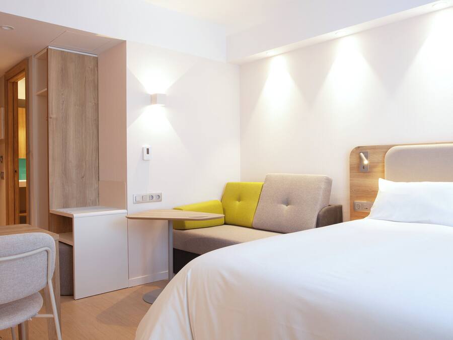 Quarto de hotel moderno com cama, escrivaninha e área de estar.