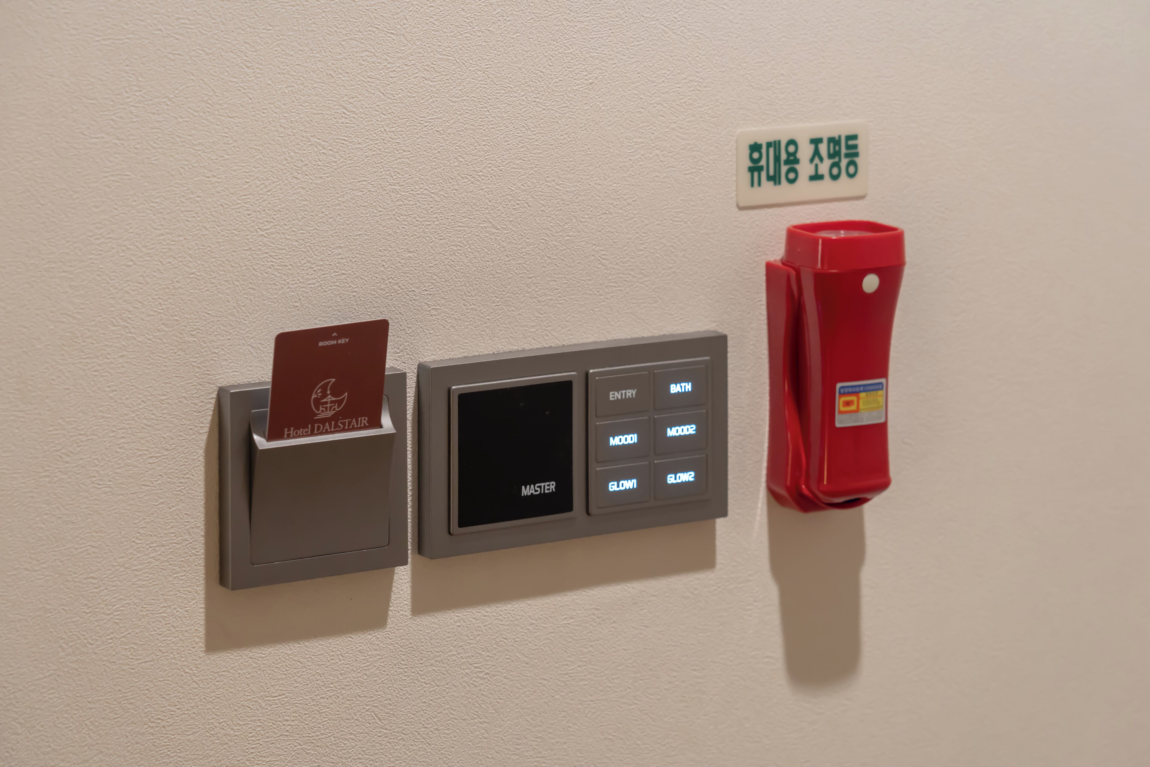 Painel de controle de um quarto de hotel, com leitor de cartão, visor digital e botão de emergência vermelho.