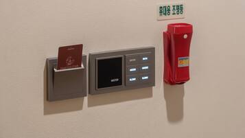 Painel de controle de um quarto de hotel, com leitor de cartão, visor digital e botão de emergência vermelho.