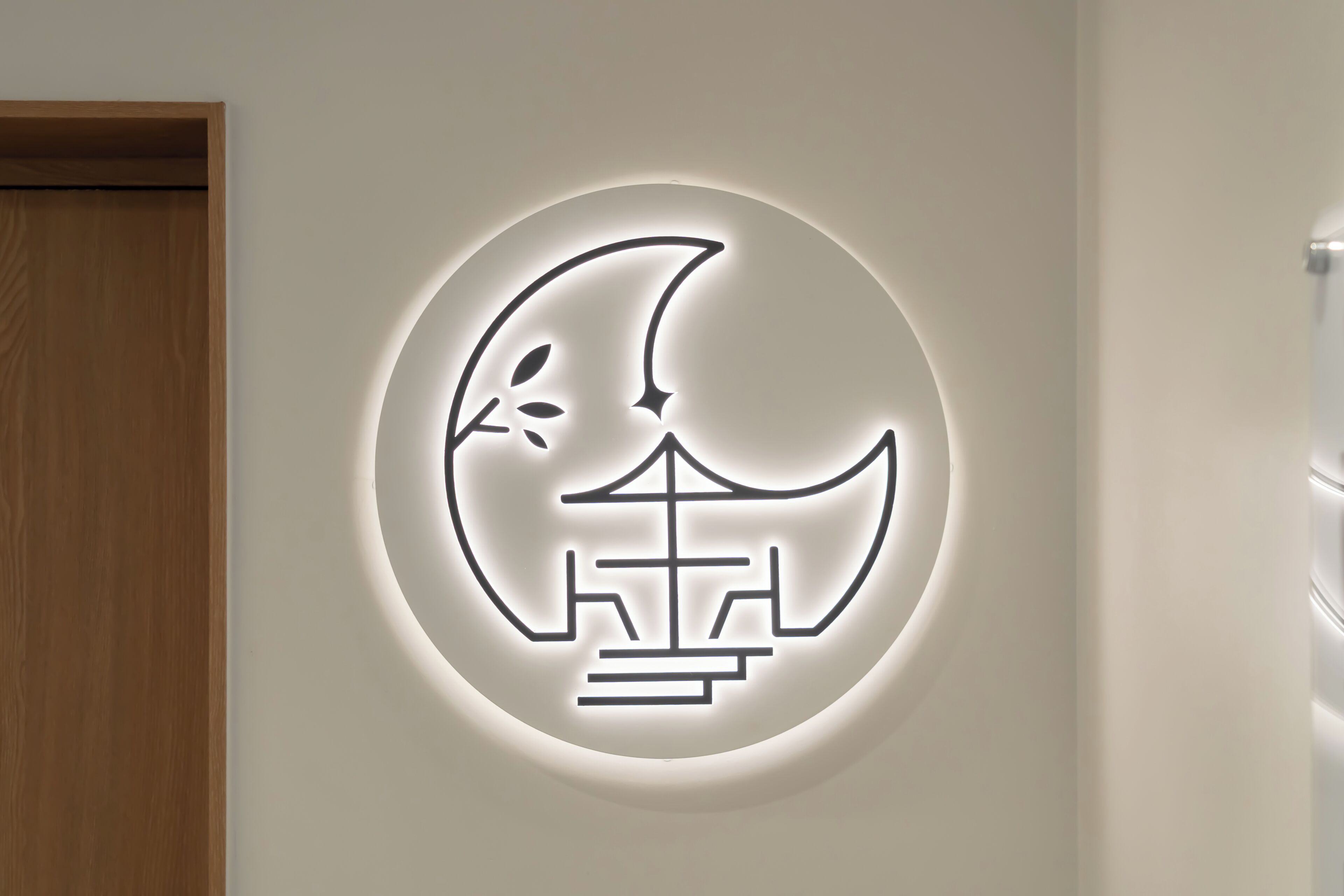 Arranjo de luz circular fixado na parede, com design que lembra uma crescente lunar e um pagode japonês tradicional.