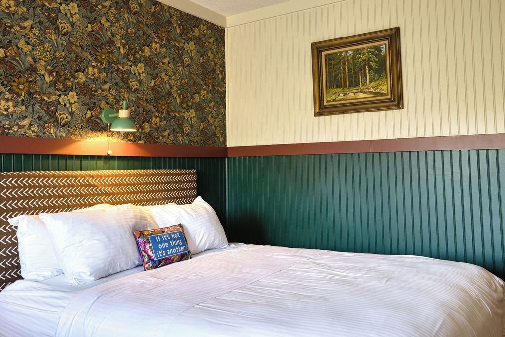 Quarto de hotel com uma cama, papel de parede floral, uma moldura na parede e cabeceira verde.