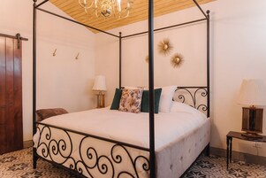 Uma cama de dossel com colchão branco e almofadas verdes e brancas, teto de madeira e soalho estampado.