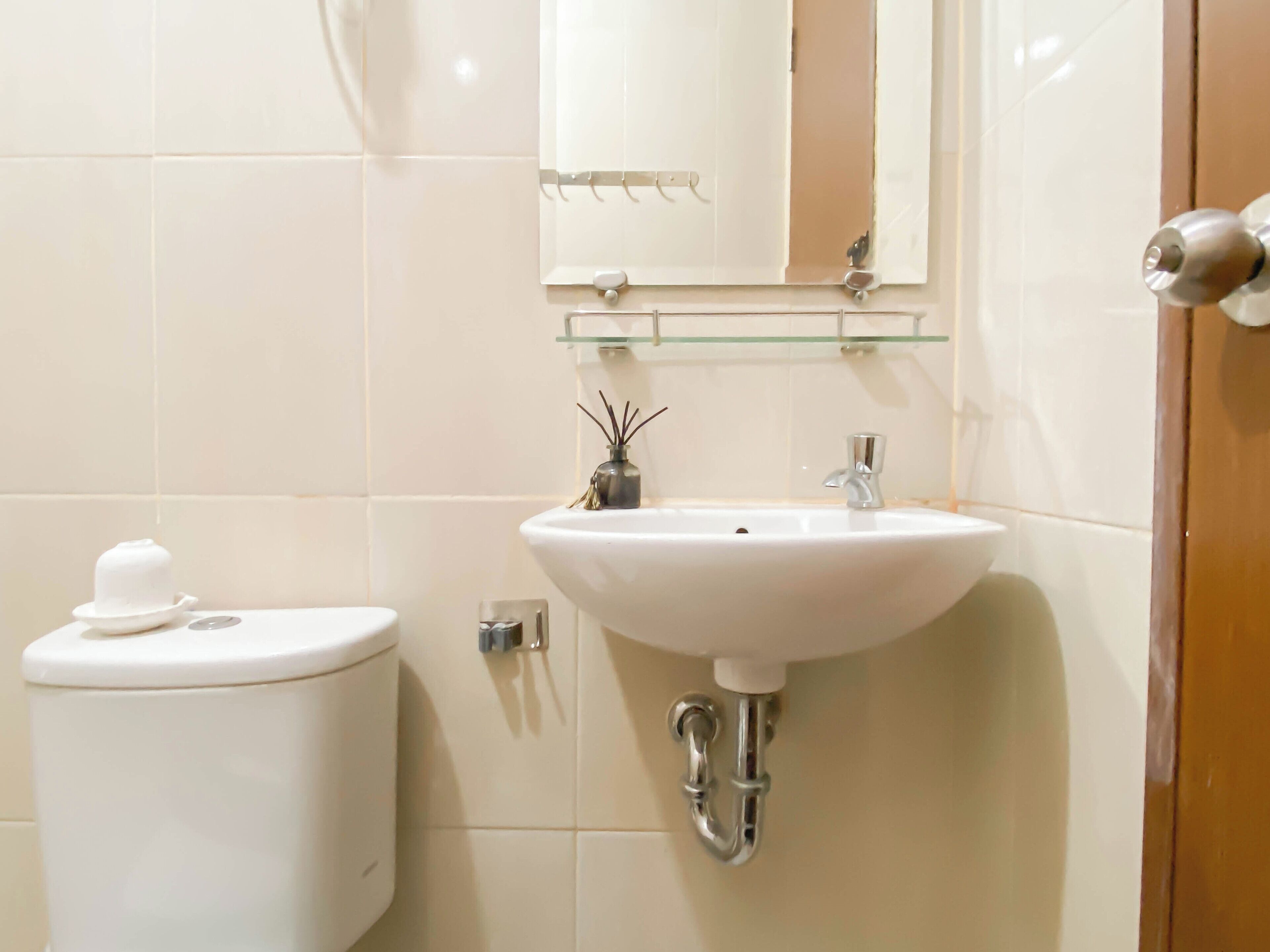 Casa de banho com sanita branca, lavatório branco e prateleira de vidro acima do lavatório.