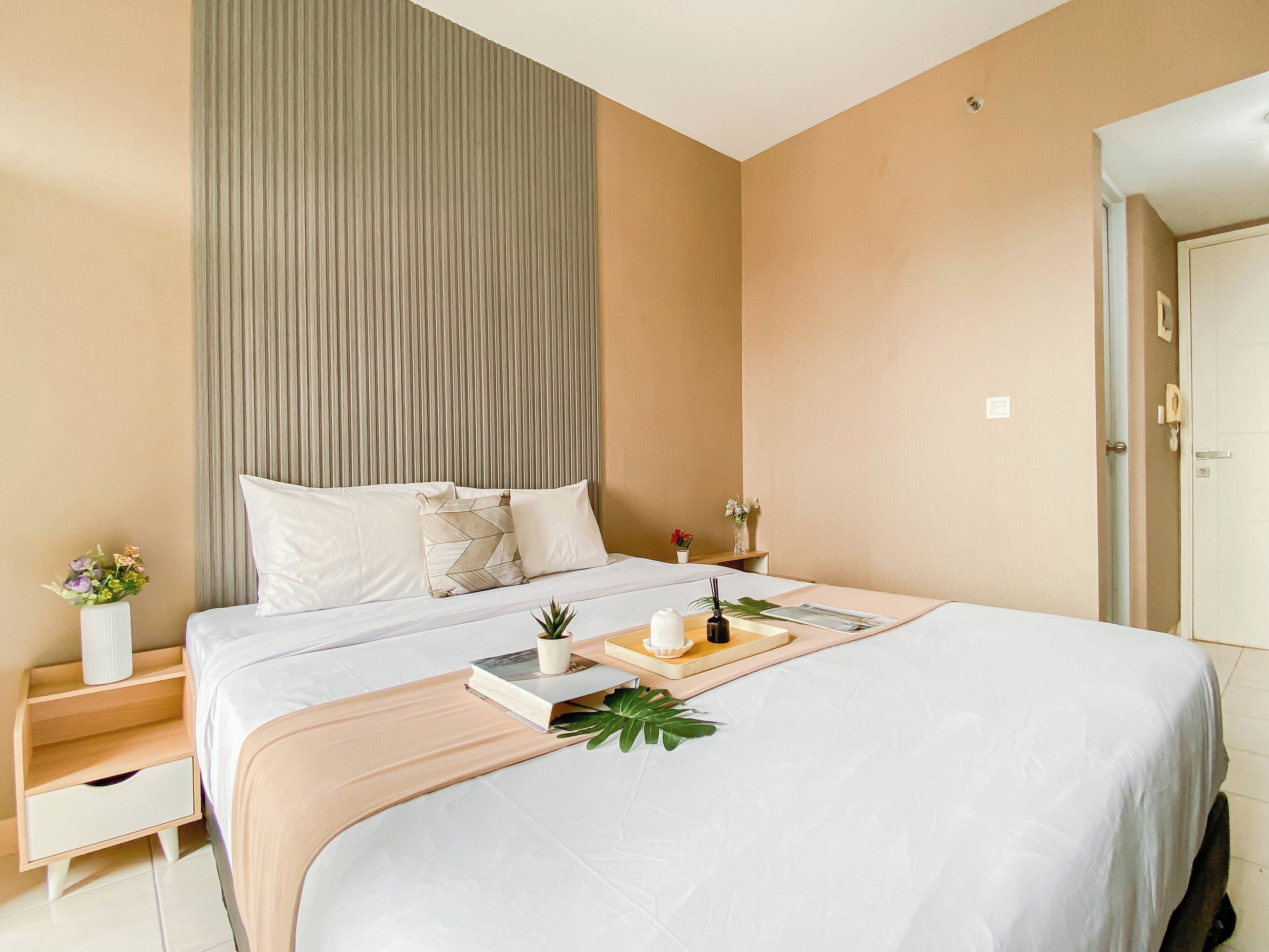 Quarto de hotel moderno com uma cama grande, uma mesa de cabeceira e um painel fixado na parede.