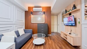 Uma sala de estar moderna com um sofá cinza, uma mesa de centro branca, uma TV fixada na parede e um armário de madeira.