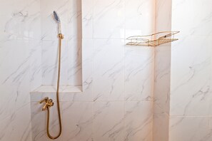 Um banheiro com chuveiro dourado, porta-toalhas fixado na parede e parede revestida com mármore.