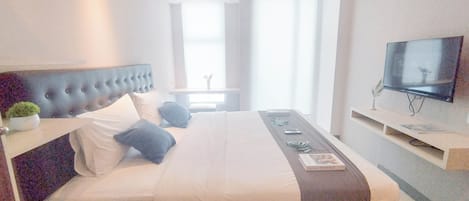 Quarto de hotel moderno com uma cama grande, uma televisão de tela plana e vista para o exterior.