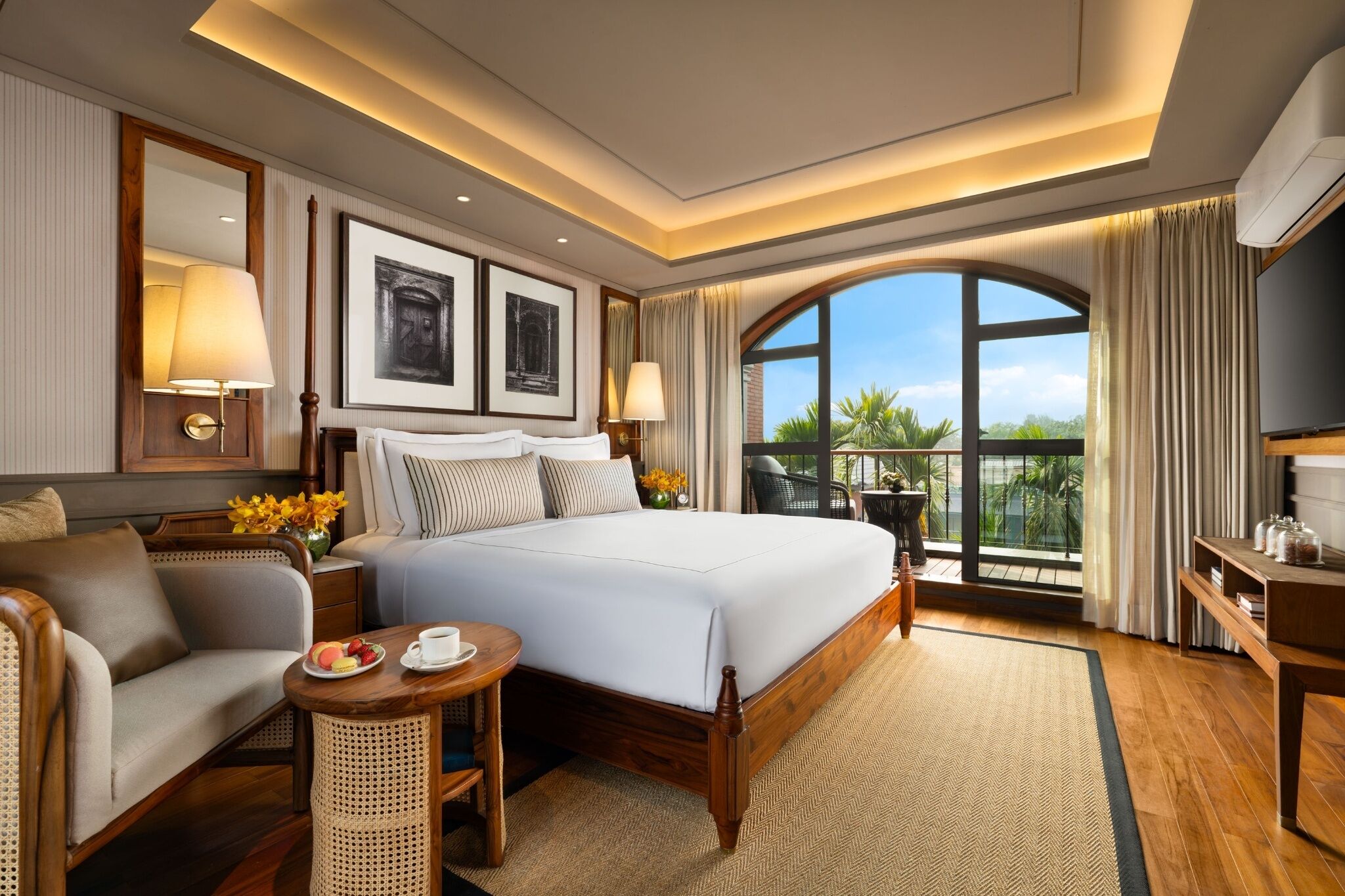 Quarto de hotel com uma cama grande, um sofá, uma mesa pequena com uma chávena e um prato, e uma varanda com vista.