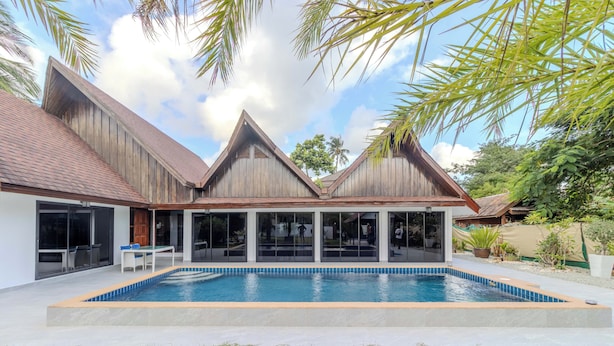 Uma casa moderna com piscina, grandes janelas de vidro e área de varanda coberta.