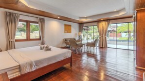 Um quarto espaçoso com uma cama grande, piso de madeira, um espaço de estar com cadeiras e vista para o exterior através de amplas janelas.