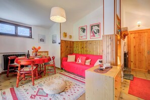 Uma sala de estar aconchegante com um sofá vermelho, paredes de madeira, uma mesa de jantar com cadeiras e uma janela grande.
