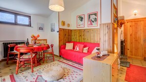 Um quarto aconchegante com um sofá vermelho, paredes de painel de madeira, uma mesa de jantar com cadeiras, um lustre pendurado e um pequeno armário de madeira.