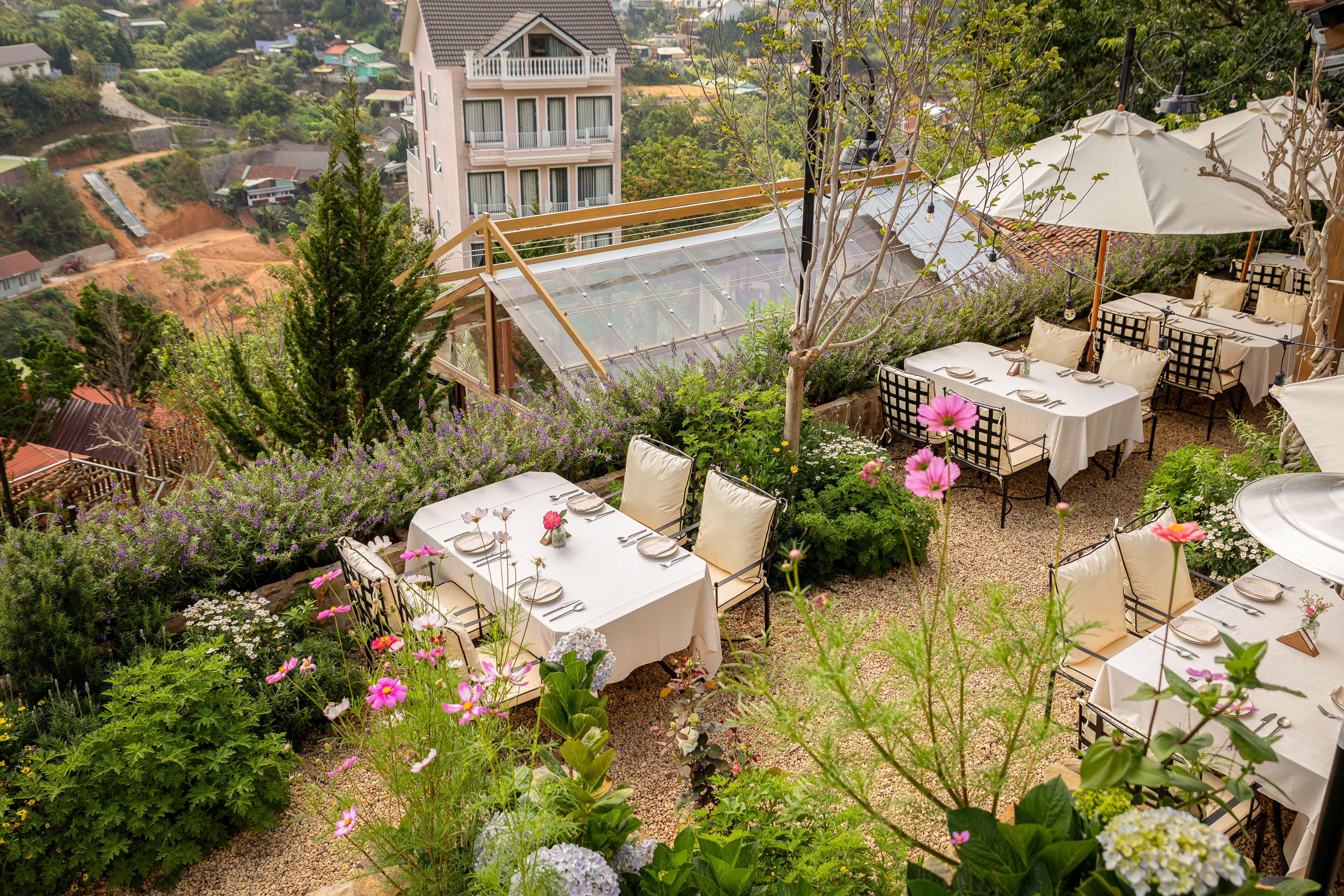 Um jardim no terraço com mesas e cadeiras, cercado por vegetação exuberante e flores.