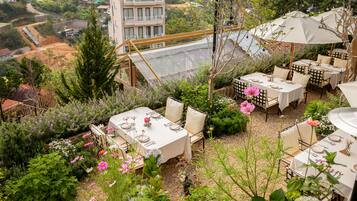 Um jardim no terraço com mesas e cadeiras, cercado por vegetação exuberante e flores.
