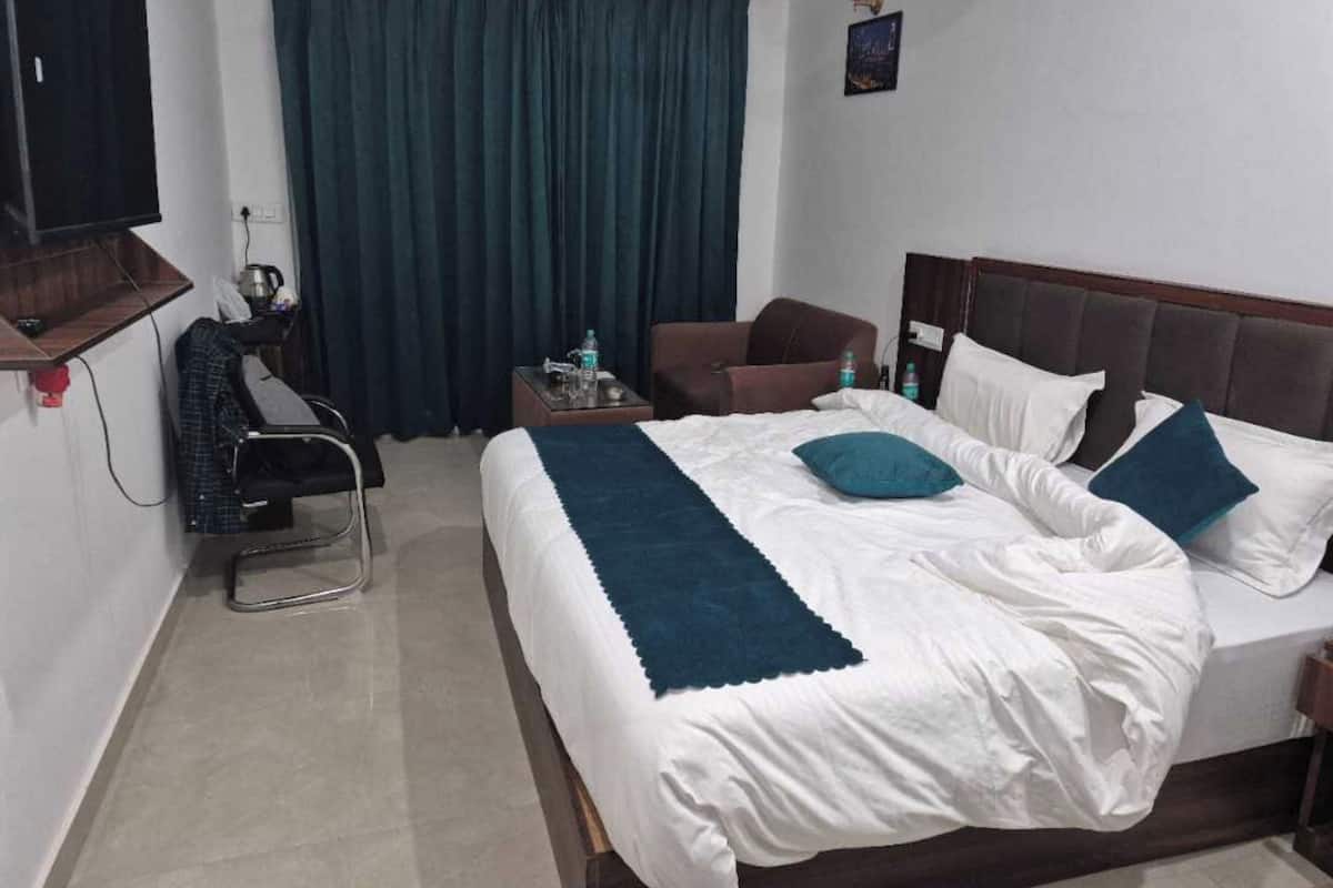 Quarto de hotel com cama, cadeira, escrivaninha, televisão e janela com cortinas.