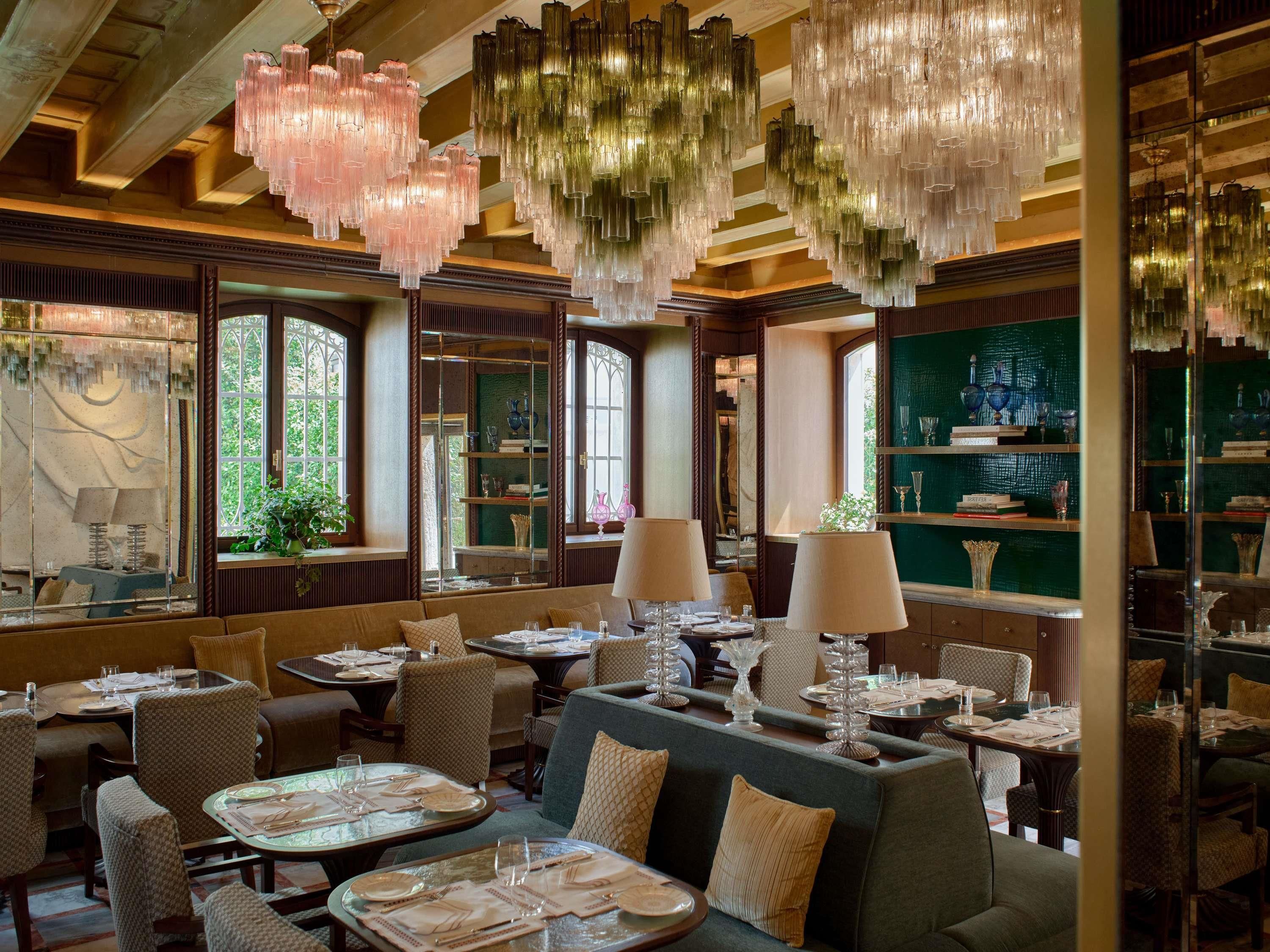 Interior de restaurante com várias mesas, cadeiras e lustres pendurados.