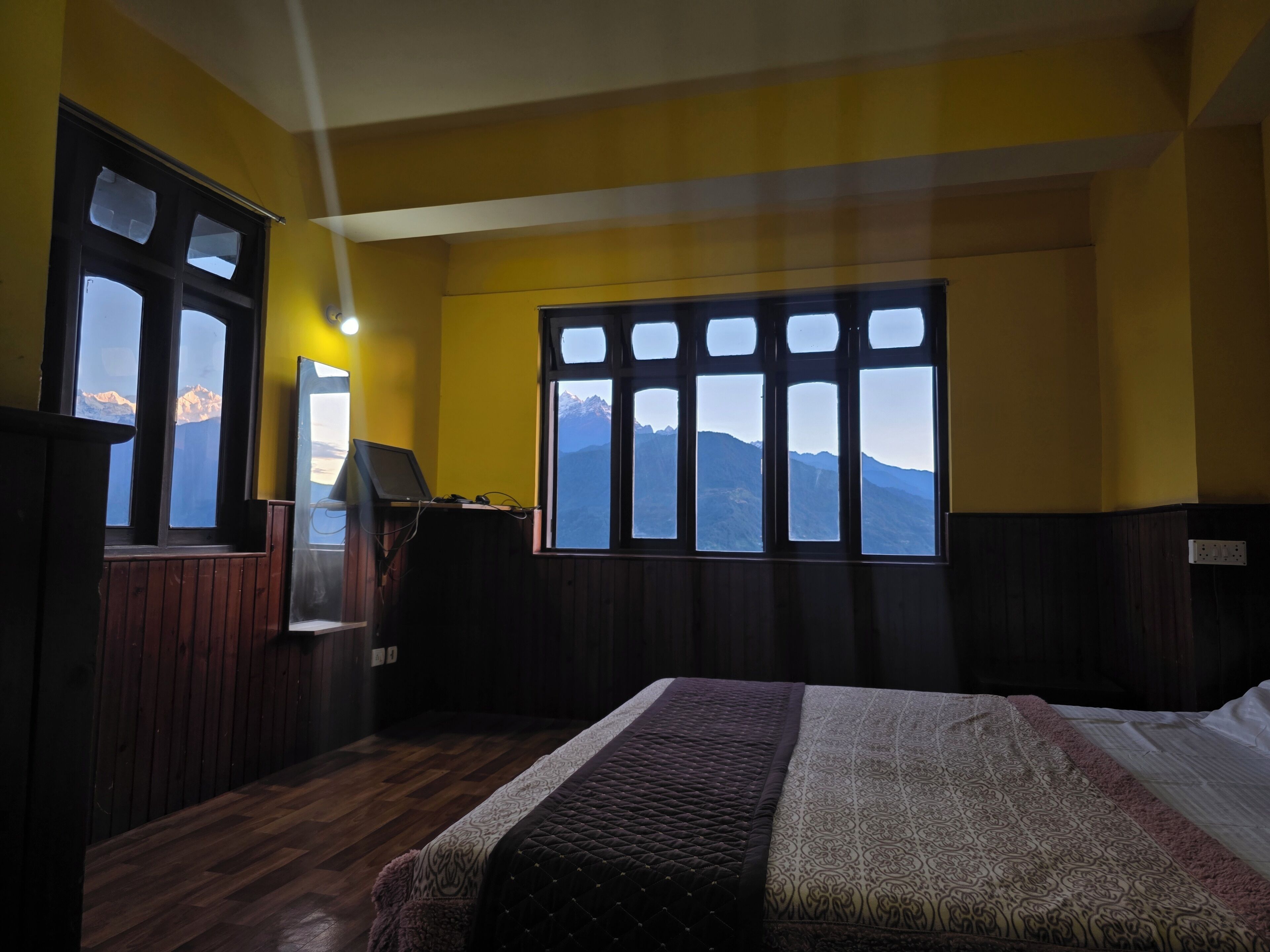 Quarto com cama, escrivaninha e janela com vista para as montanhas.