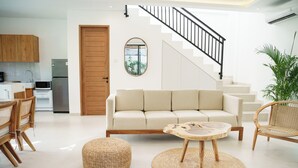 Uma sala de estar moderna com sofá, mesa de centro e cadeiras. Uma escada com corrimão preto leva a um andar superior.