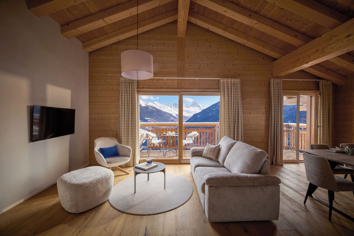Uma cabana de madeira aconchegante com uma grande janela que oferece vista para as montanhas, uma TV de tela plana e um espaço de jantar com mesa e cadeiras.