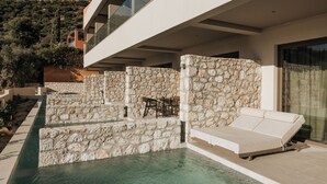 Uma área de piscina moderna ao ar livre, com paredes de pedra e uma espreguiçadeira.